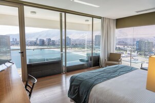 Quarto de hotel com uma cama grande, uma escrivaninha, uma cadeira e vista para a cidade e montanhas.