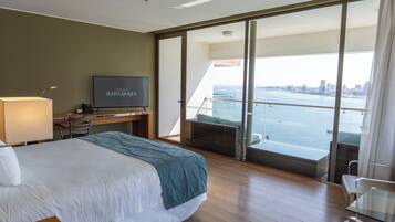 Quarto de hotel com cama, escrivaninha com televisão, vista para o mar e varanda.