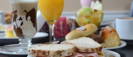 Uma mesa de café da manhã com sanduíches, um copo de suco de laranja e uma tigela de frutas.