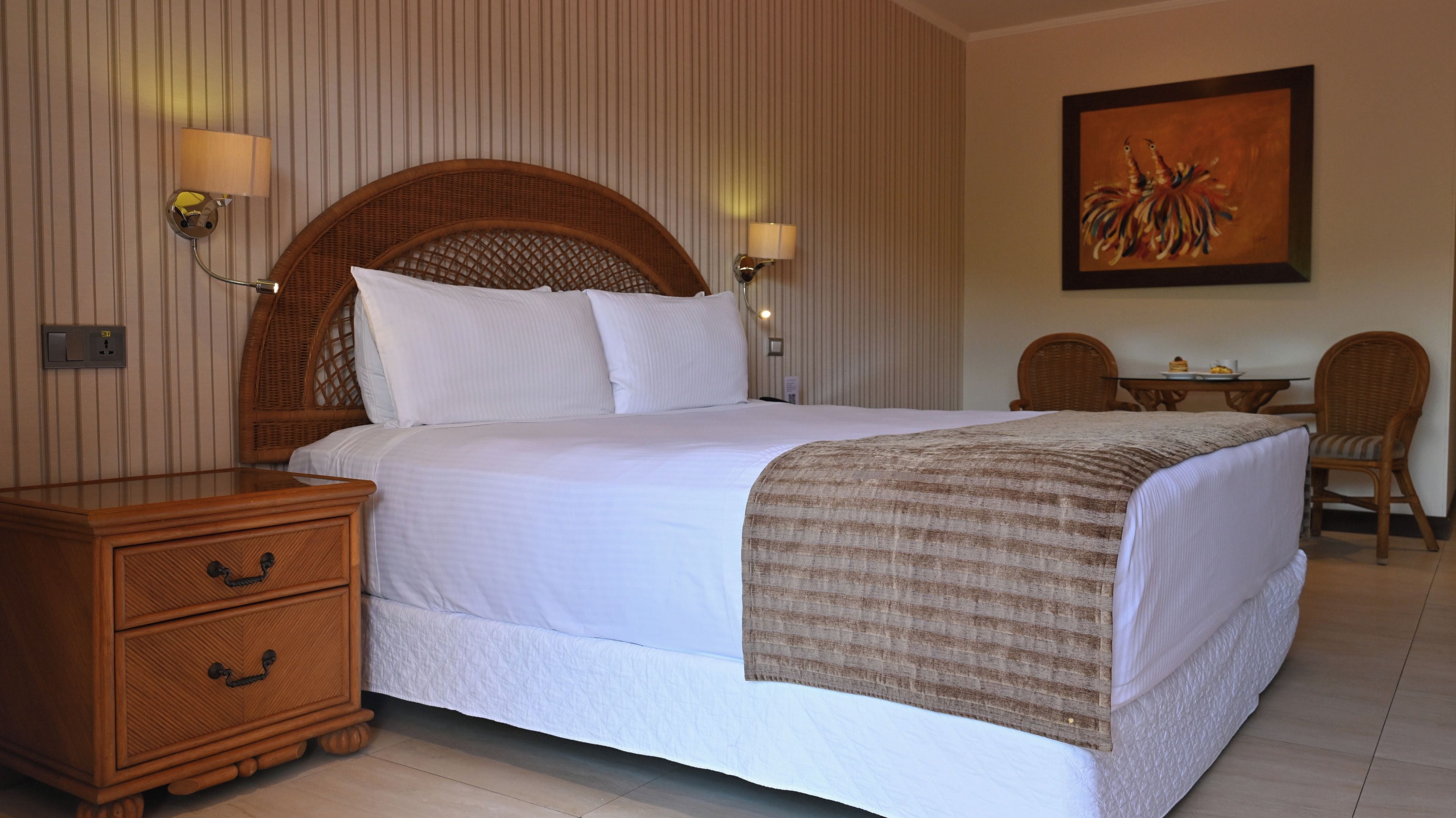 Quarto de hotel com cama grande, mesas de cabeceira, escrivaninha e cadeiras.