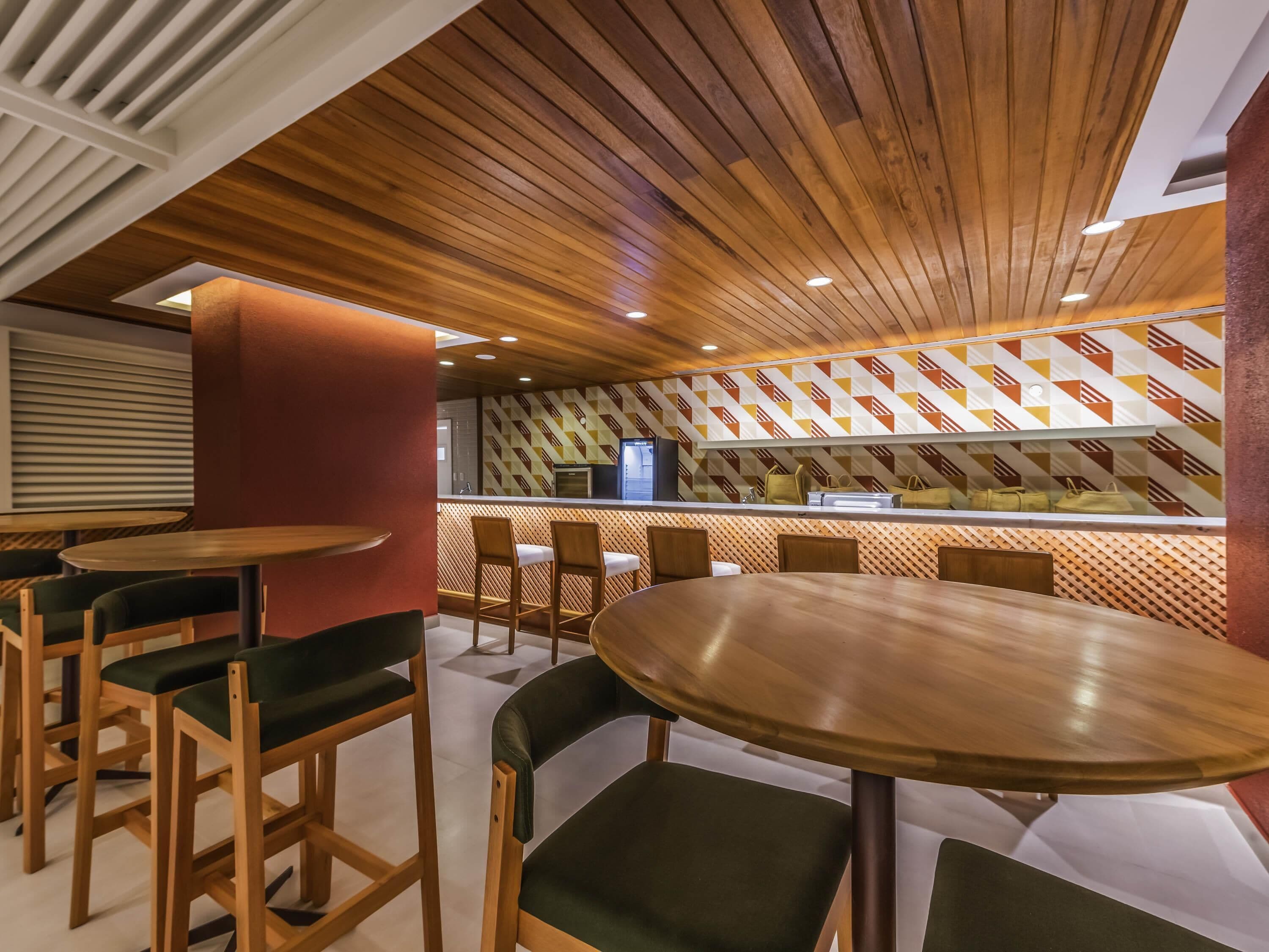 Interior de restaurante com painéis de teto de madeira, parede estampada e diversas áreas de estar.