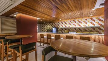 Interior de restaurante com painéis de teto de madeira, parede estampada e diversas áreas de estar.