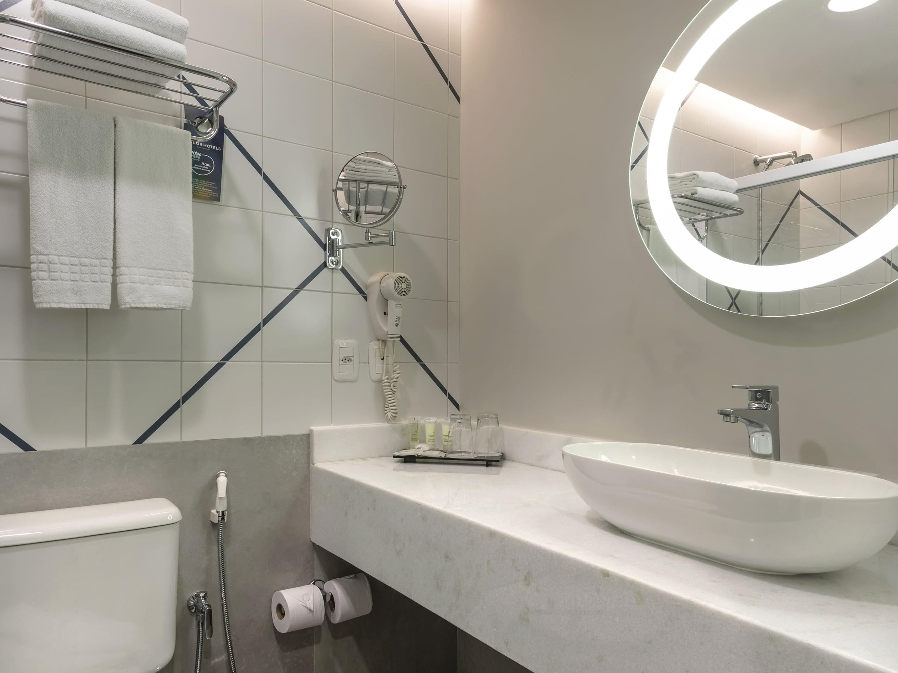 Casa de banho com sanita, bidé, porta-toalhas, secador de cabelo e lavatório com espelho.