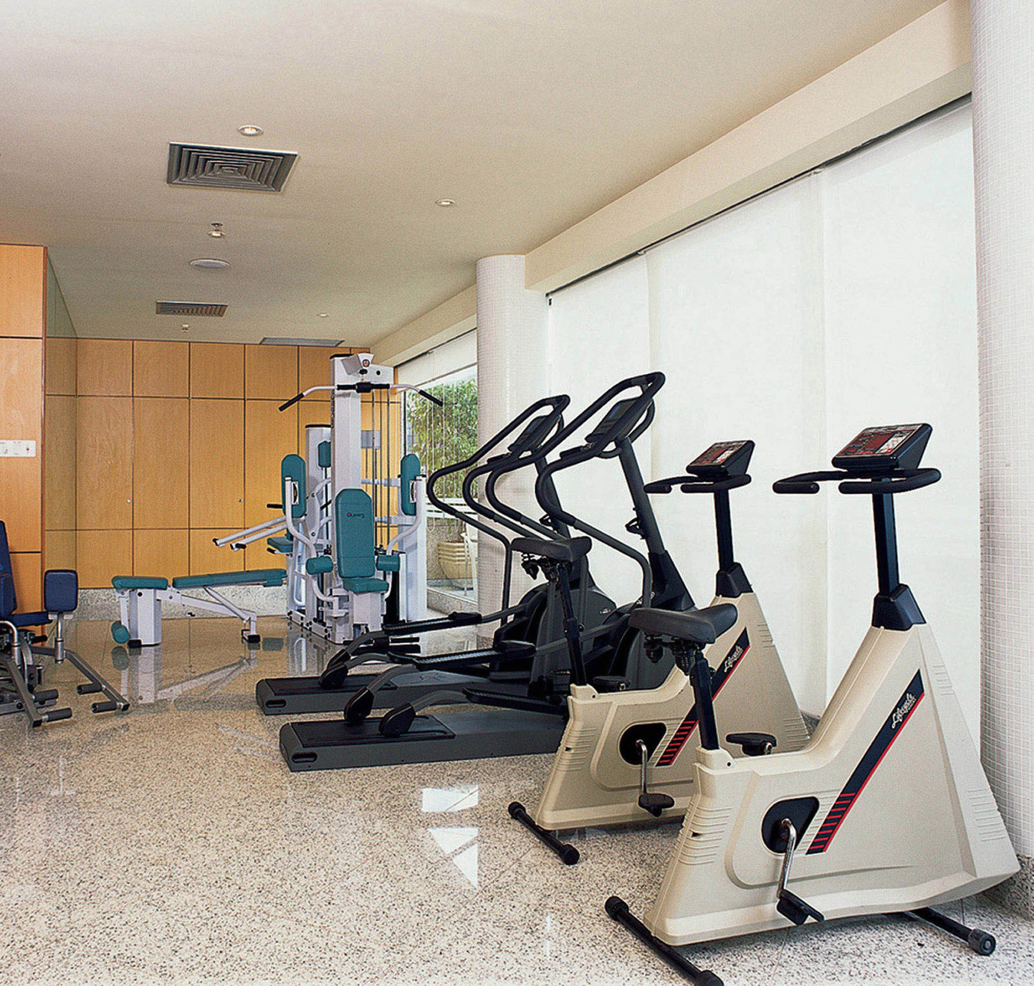 Uma academia com bicicletas ergométricas, um aparelho de musculação e um espelho.