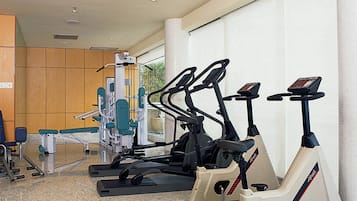 Uma academia com bicicletas ergométricas, um aparelho de musculação e um espelho.