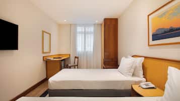 Quarto de hotel com cama, escrivaninha, cadeira, televisão e um quadro na parede.