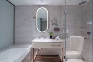 Um banheiro moderno com um espelho oval grande, uma banheira, área de chuveiro e um porta-toalhas com uma toalha da marca 'HOTEL'.