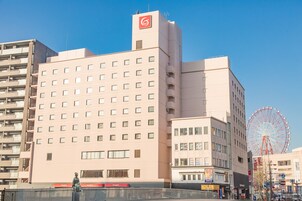 Um hotel de vários andares com um logotipo vermelho chamativo no topo, uma grande roda gigante ao fundo e uma estátua em frente.