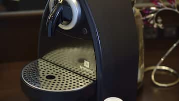 Uma máquina de café Nespresso com uma bandeja coletora, uma xícara de metal e uma colher sobre uma mesa de madeira.