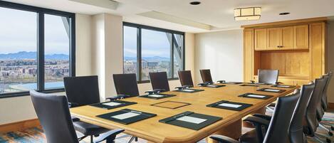 Sala de conferências com uma grande mesa, cadeiras e vista para a cidade através de amplas janelas.