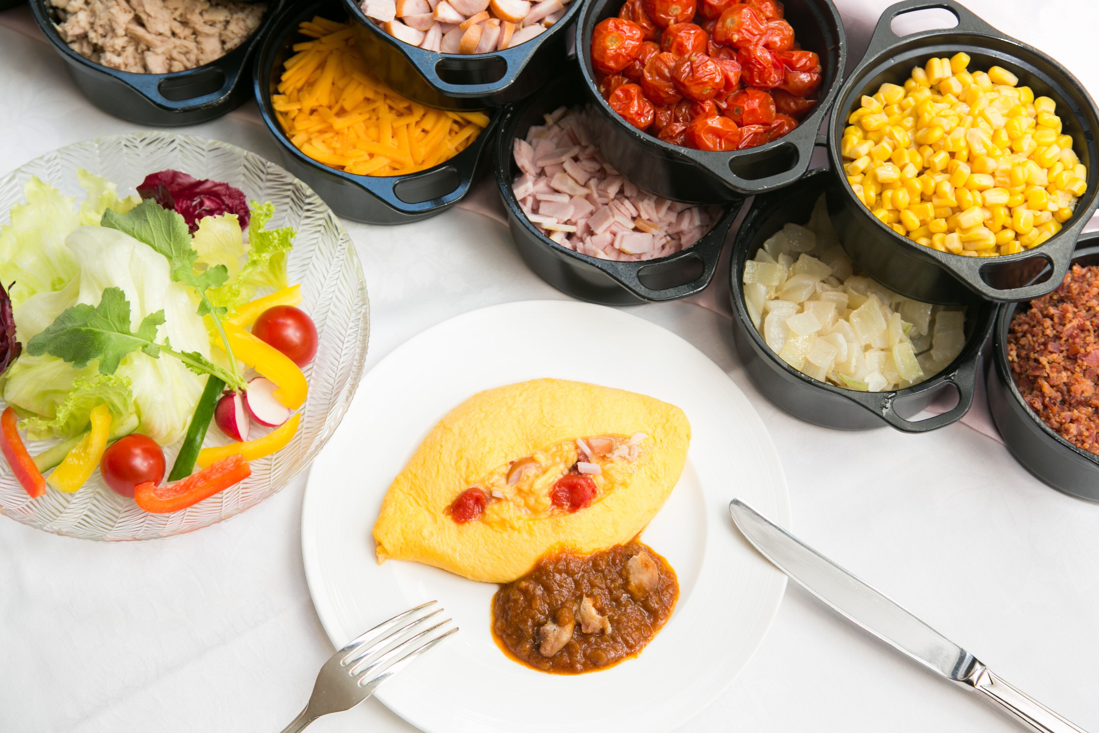 Diversos tipos de alimentos, incluindo um prato com salada, uma tigela de milho e vários recipientes com diferentes ingredientes.