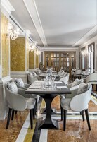 Uma sala de jantar formal com uma mesa grande, cadeiras acolchoadas e lustres.
