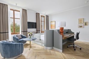 Quarto de hotel moderno com sofá, escrivaninha, cadeira, televisão e janela com cortinas.