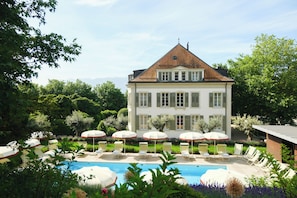 Um edifício amplo com piscina, rodeado por vegetação e área de estar externa.