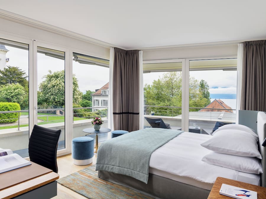 Quarto de hotel moderno com uma cama grande, uma mesa pequena e uma varanda com vista para a cidade.