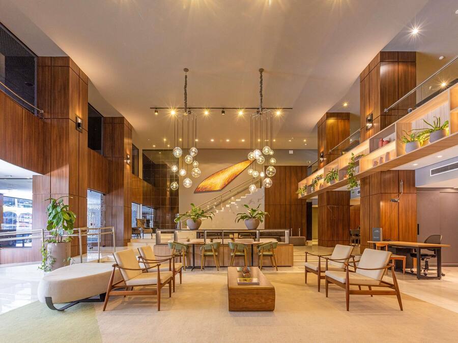 Um hall amplo com área de estar central, painéis de madeira e luminárias esféricas penduradas.