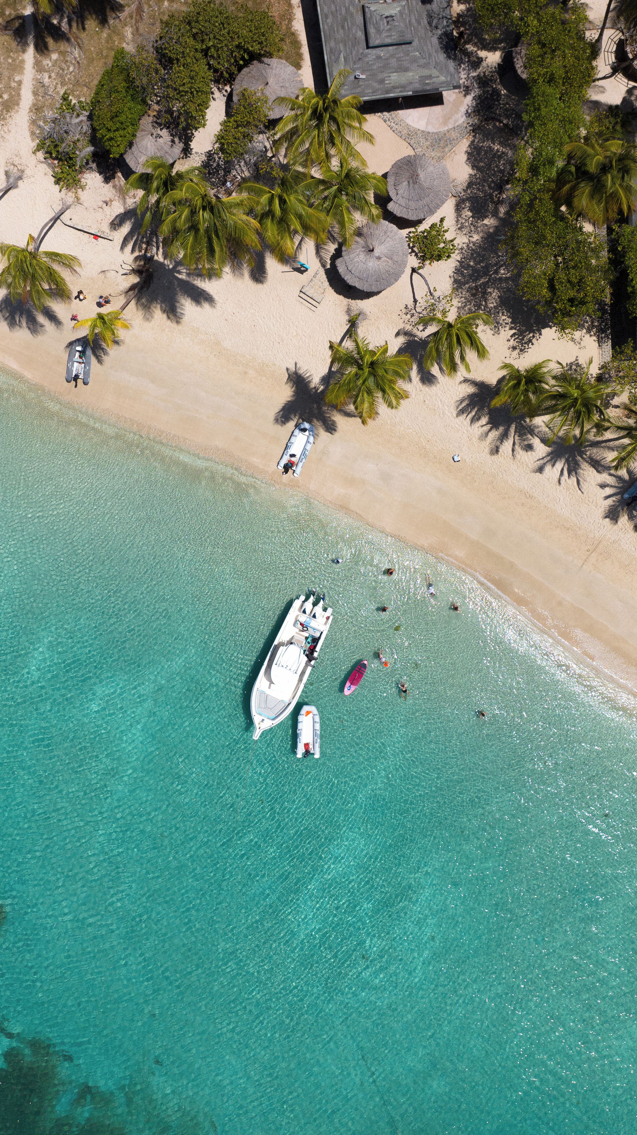 Vista aérea de uma praia com água turquesa cristalina, um barco e algumas pessoas.