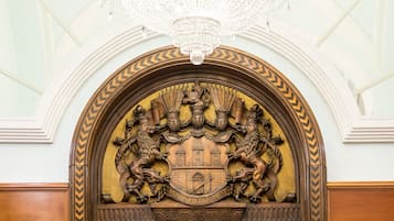 Um brasão detalhado com leões e um castelo, inserido numa moldura em arco com um candelabro acima.