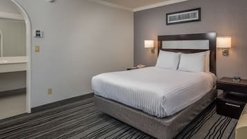 Quarto de hotel com uma cama grande, duas mesas de cabeceira, um criado-mudo, telefone fixado na parede e um quadro emoldurado sobre a cama.