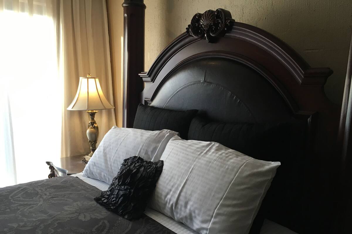 Cama bem arrumada com colcha estampada, duas almofadas brancas e uma almofada decorativa preta.