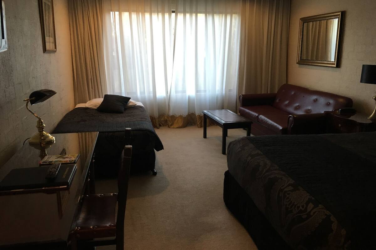 Quarto de hotel com cama, sofá, escrivaninha com luminária e televisão.