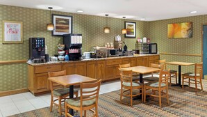 Uma cozinha de hotel com armários de madeira, um espaço para café e uma área de refeições com mesas e cadeiras.