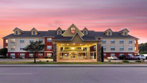 Um hotel com entrada central, vários andares e estacionamento.