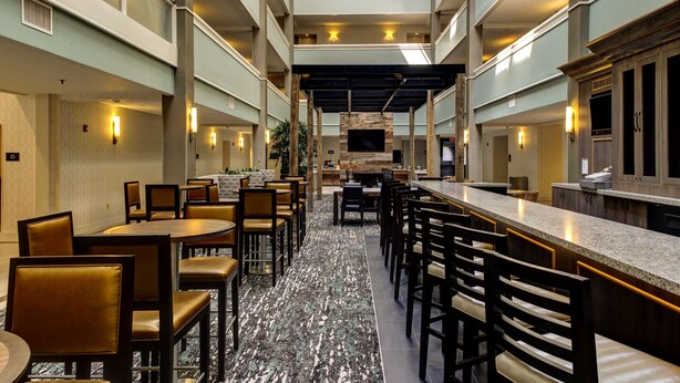Um saguão de hotel com várias áreas de refeições, um bar central e uma tela de TV.