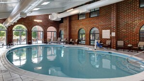 Piscina interna com parede de tijolos, janelas em arco e espreguiçadeiras.
