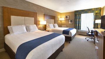 Quarto de hotel com duas camas, uma escrivaninha, uma cadeira e uma televisão.