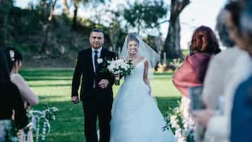 Uma cerimônia de casamento ao ar livre, com uma noiva e um noivo caminhando pelo corredor.