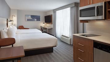 Quarto de hotel com cama, escrivaninha, cadeira, micro-ondas e forno embutido.