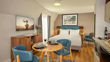 Quarto de hotel com cama, escrivaninha, cadeira, pequena mesa com um vaso de flores e um quadro na parede.