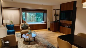 Uma sala de estar moderna com um sofá, uma mesa de centro, um rack para TV e uma janela com vista para o verde.