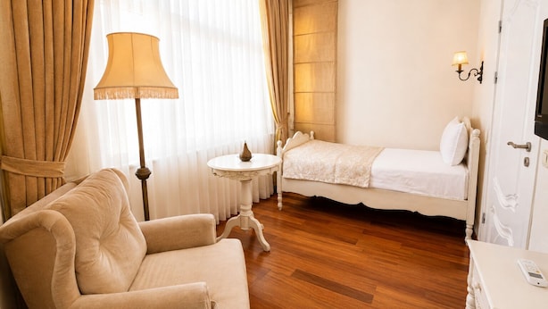 Quarto de hotel com uma cama de solteiro, uma cadeira, uma mesa e um abajur.