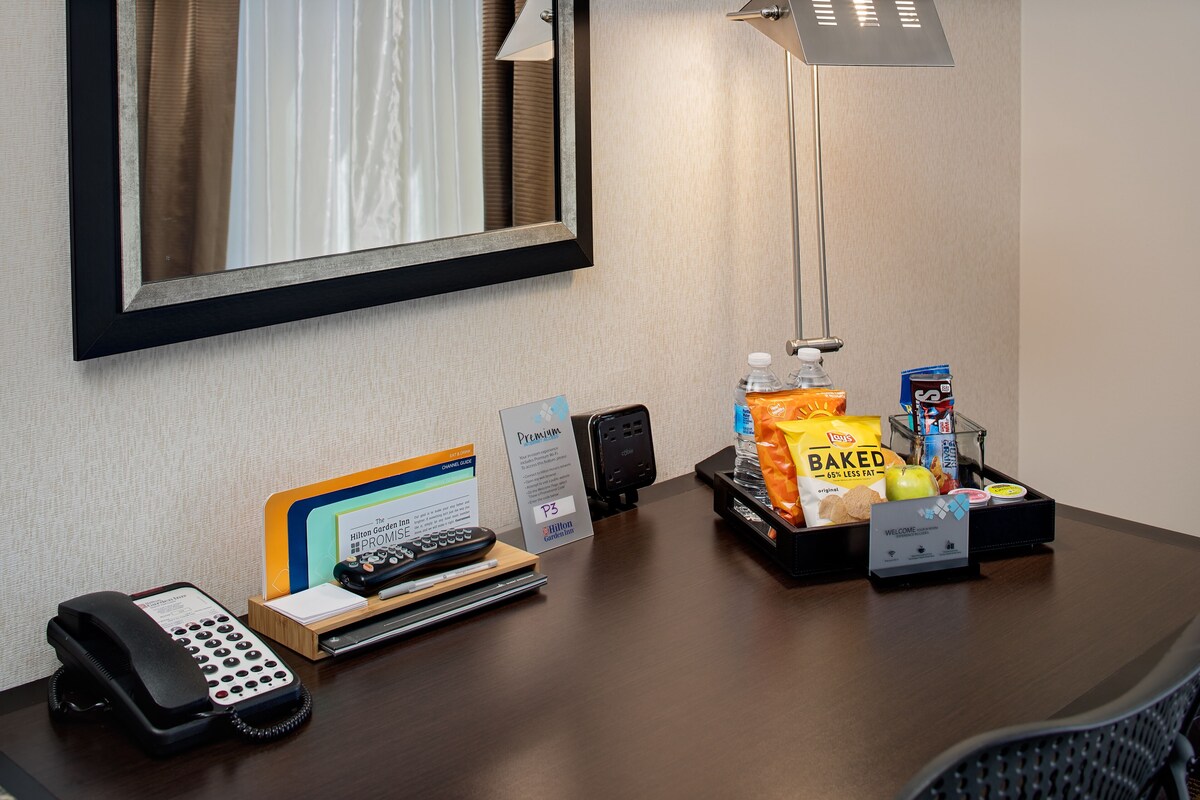 Balcão de hotel com telefone, bloco de notas, dispositivo digital, bandeja com lanches e placa indicando quarto premium.