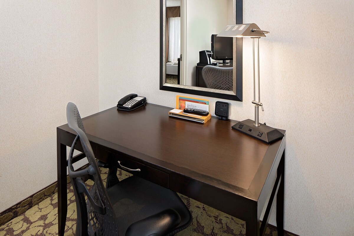Mesa de hotel com um telefone, um controle remoto, uma luminária e um espelho.
