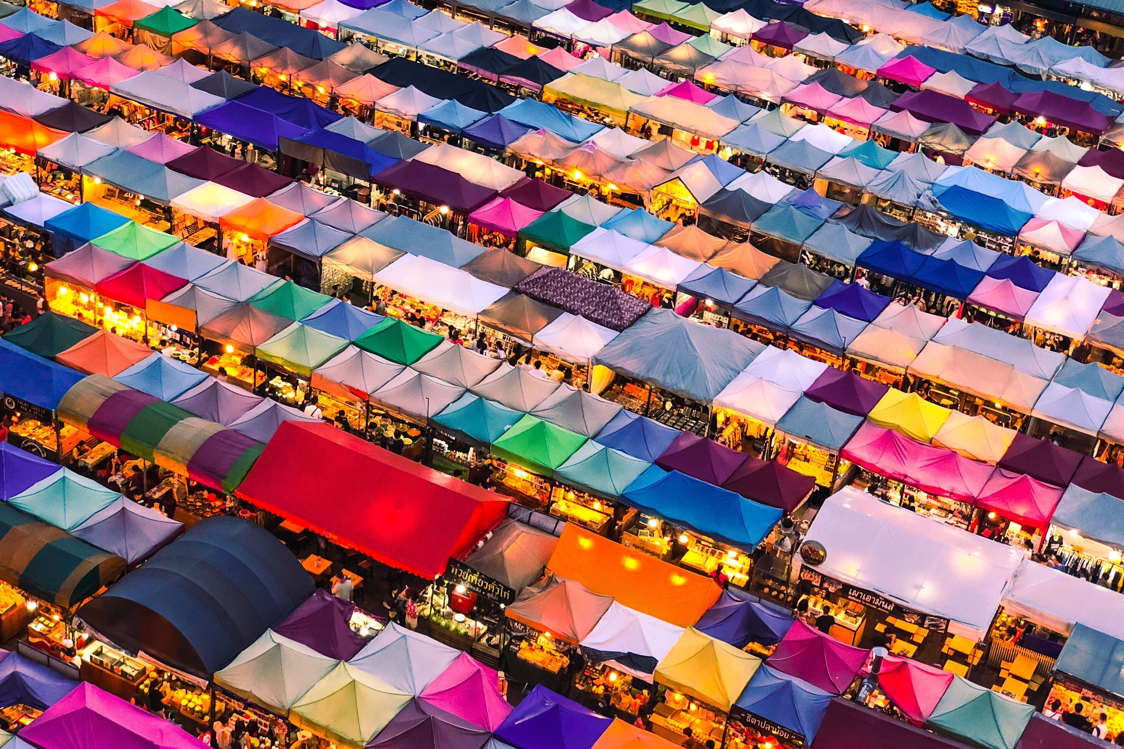 Um grande mercado ao ar livre com inúmeras barracas cobertas por guarda-sóis coloridos.