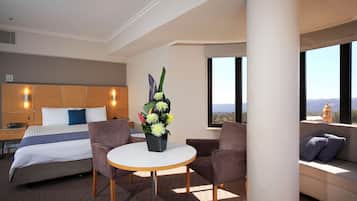 Quarto de hotel com cama, mesa redonda com cadeiras, sofá e uma janela ampla com vista.