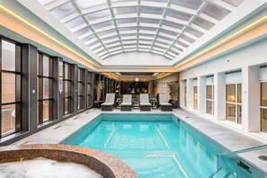 Piscina interior moderna com teto skylight, cadeiras de descanso e área de hidromassagem.