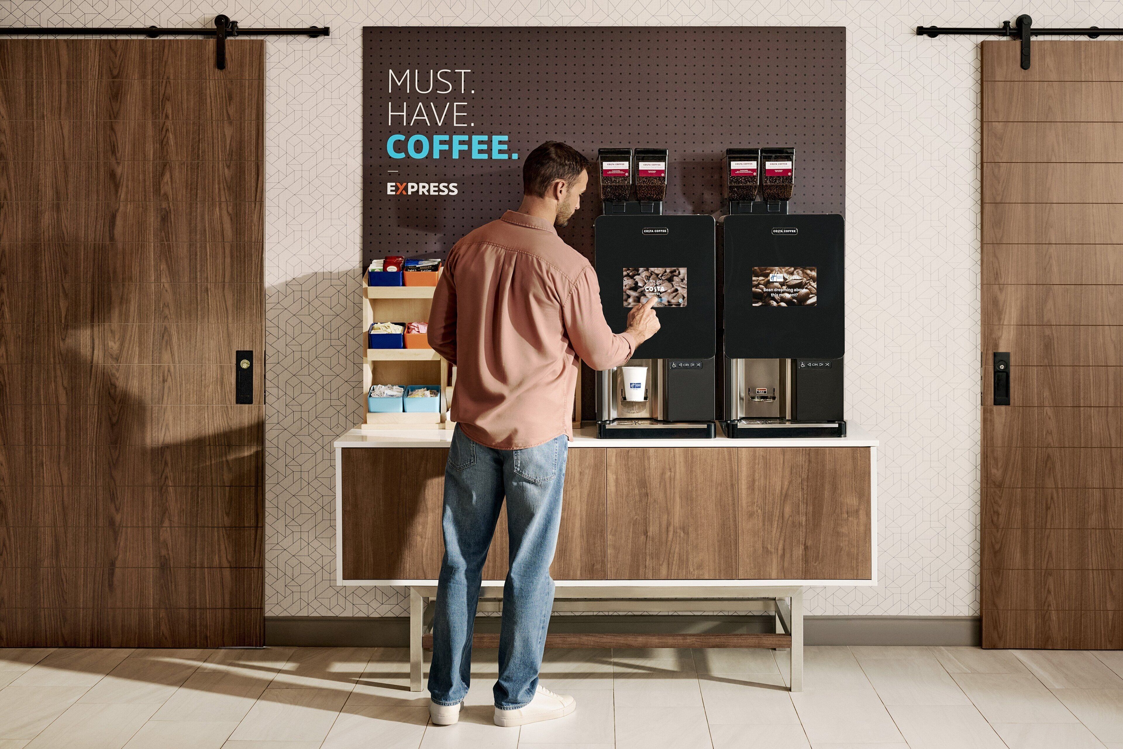 Uma pessoa em frente a um espaço com café, com uma placa que diz 'MUST HAVE COFFEE'.