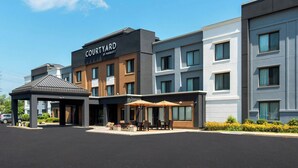 Um hotel Courtyard by Marriott com entrada coberta, área de estar ao ar livre e fachada de construção moderna.