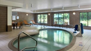 Uma piscina interior com chão em mosaico, espreguiçadeiras e grandes janelas com vista para o exterior.