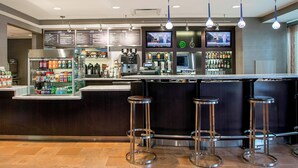Uma área de bar moderna com balcão, banquetes e uma televisão exibindo notícias.