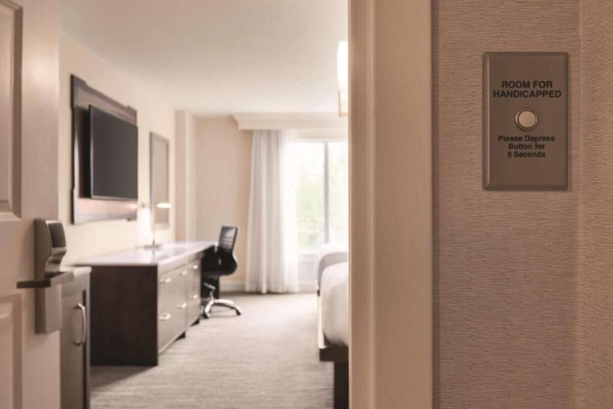 Quarto de hotel com escrivaninha, cadeira e cama. Placa indica que o quarto é para hóspedes com deficiência.