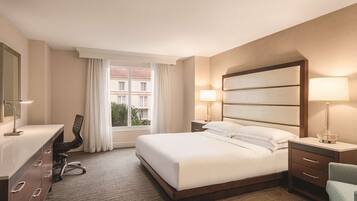 Quarto de hotel com uma cama grande, uma escrivaninha com cadeira, cómoda e duas luminárias de cabeceira.