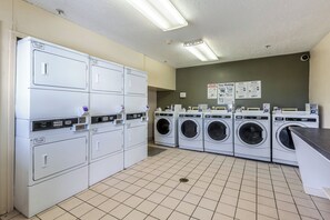 Uma lavanderia com várias máquinas de lavar e secar, piso ladrilhado e cartazes informativos na parede.