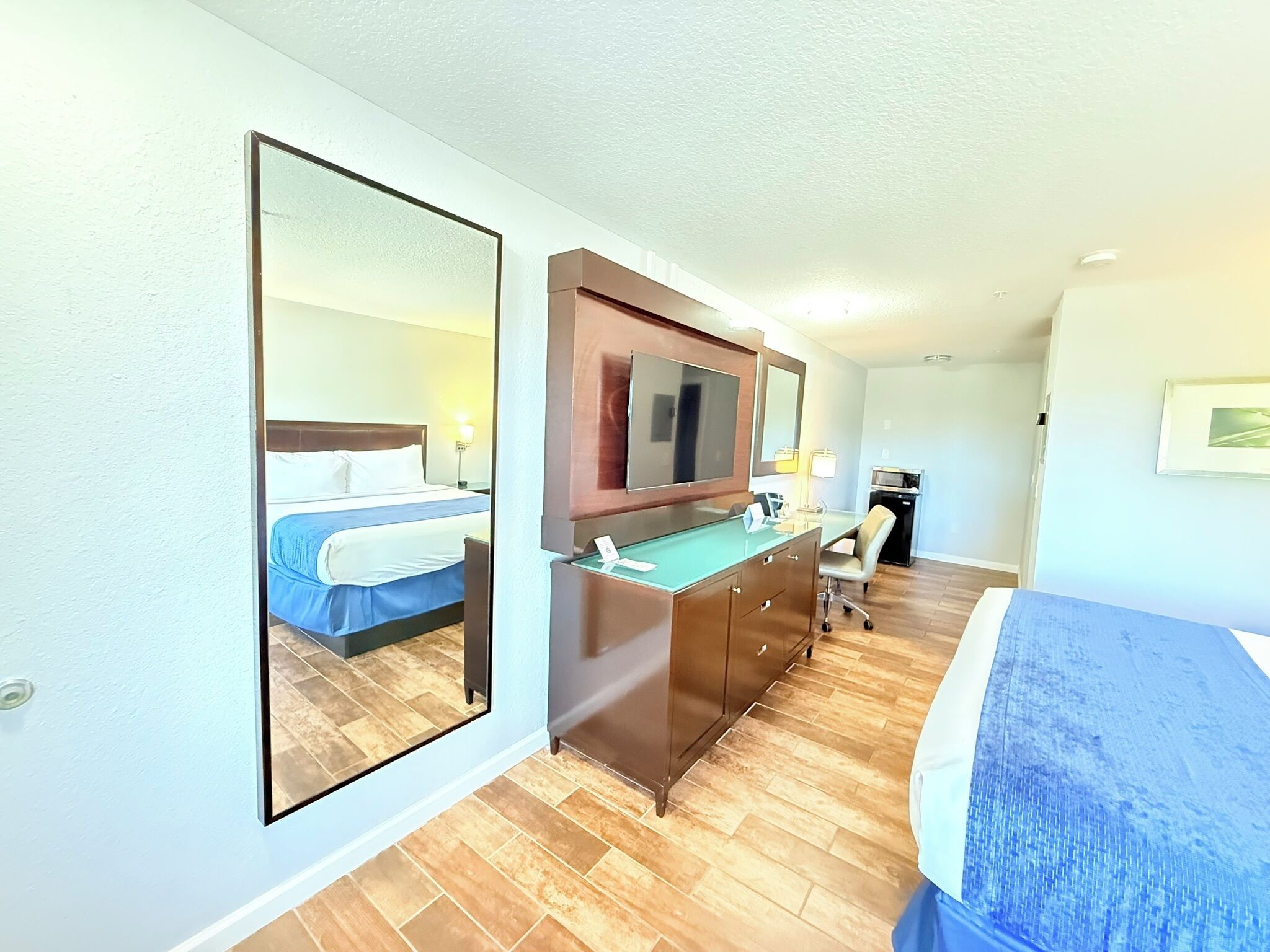 Quarto de hotel com cama, escrivaninha com espelho, cadeira e mesa pequena.