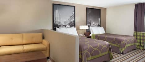 Quarto de hotel com sofá, duas camas com colchas estampadas, uma mesa de cabeceira, uma luminária e duas imagens emolduradas na parede.