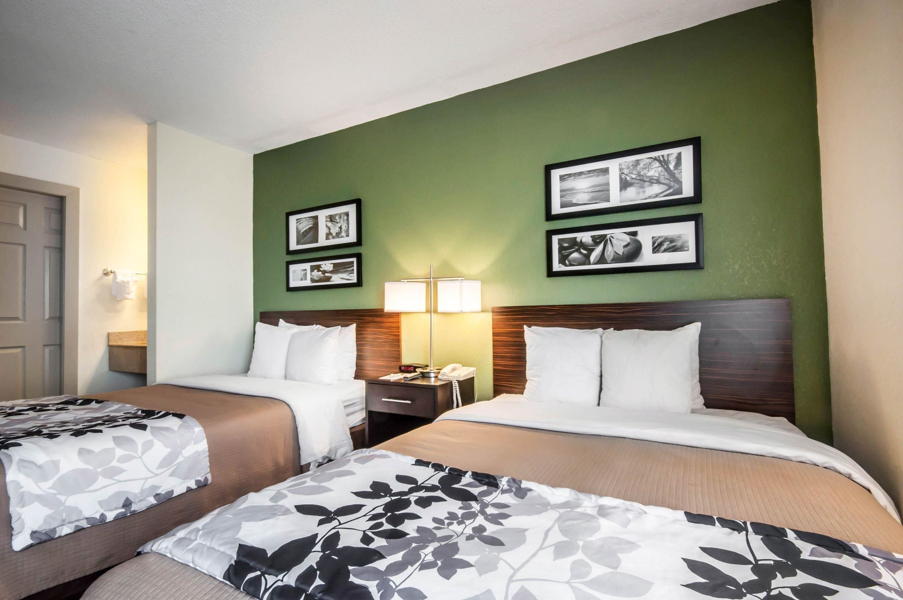 Quarto de hotel com duas camas, mesa de cabeceira com abajur e quadros nas paredes.